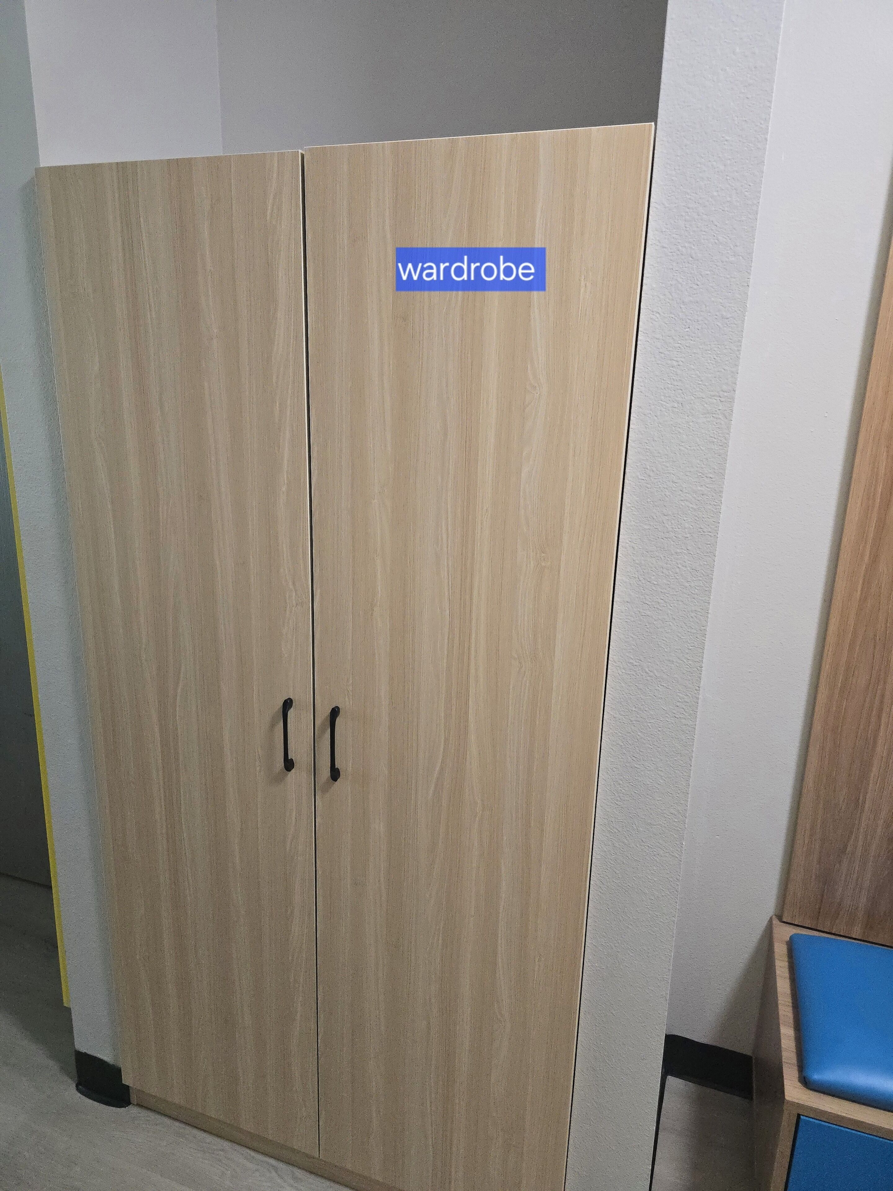 Um guarda-roupa com uma etiqueta a indicar 'wardrobe', um par de puxadores pretos e uma cadeira azul à direita.
