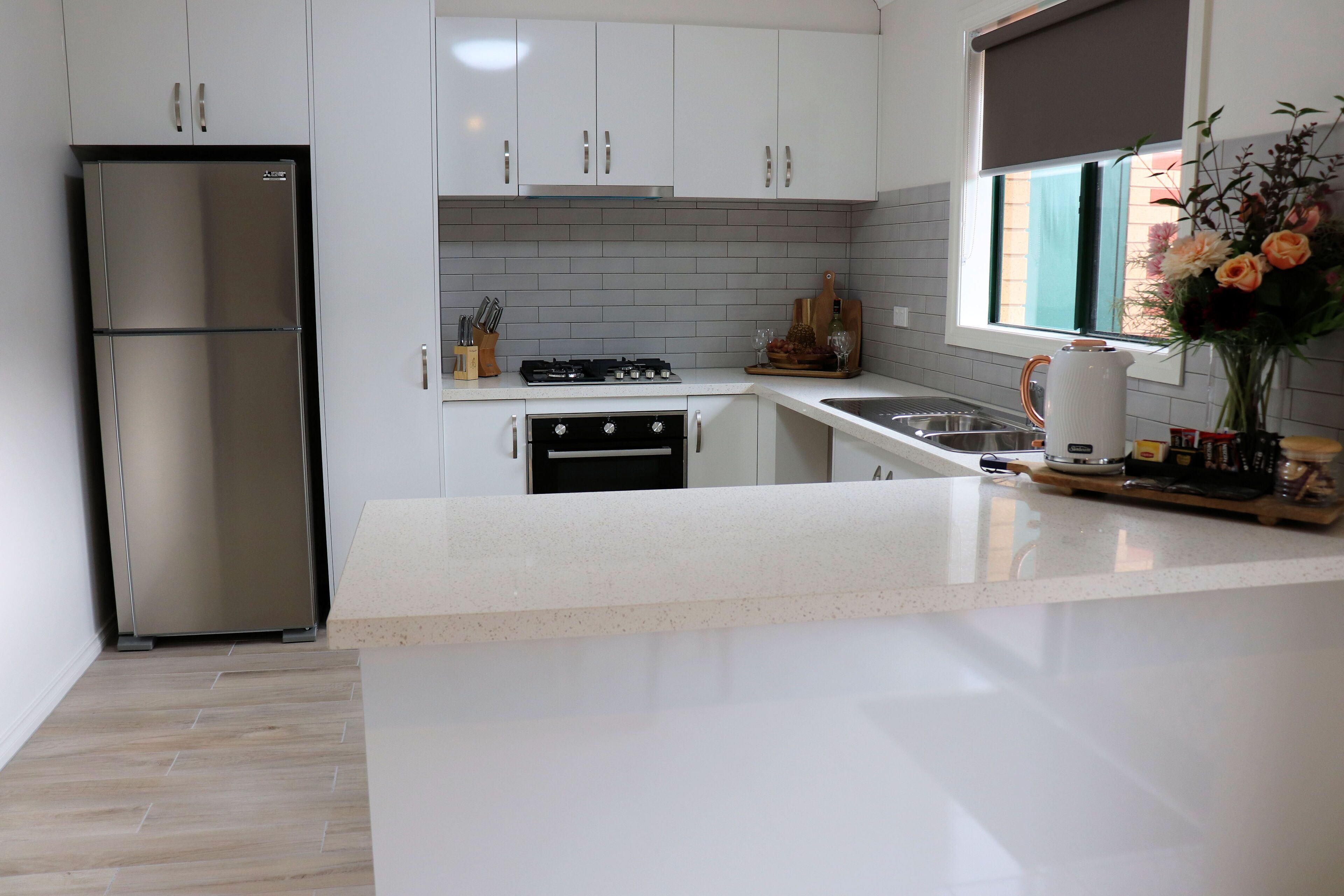 Uma cozinha moderna com armários brancos, uma geladeira de aço inoxidável, um fogão a gás e uma janela com vista.