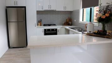 Uma cozinha moderna com armários brancos, uma geladeira de aço inoxidável, um fogão a gás e uma janela com vista.