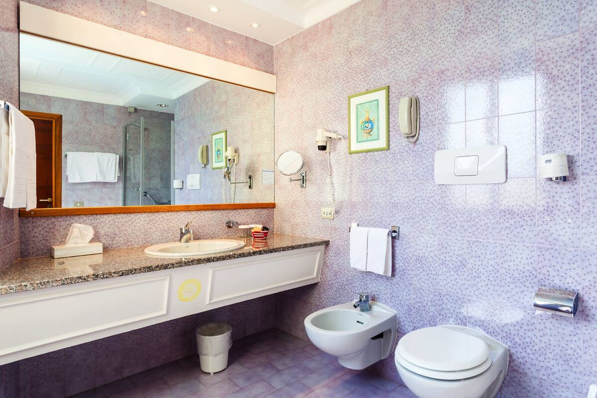 Uma casa de banho moderna com um espelho grande, duas lavatórios, um bidé e uma sanita.