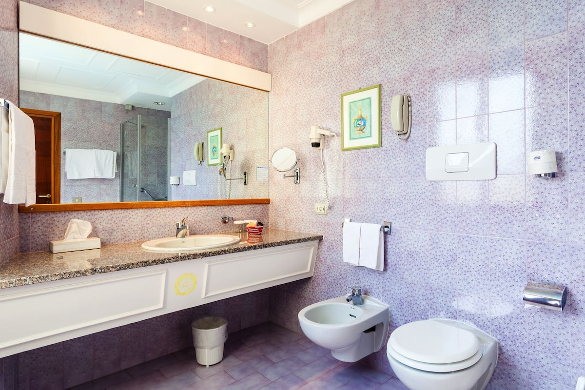Uma casa de banho moderna com um espelho grande, duas lavatórios, um bidé e uma sanita.
