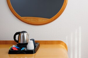 Quarto de hotel com uma mesa de madeira, uma cafeteira, uma chávena e um tabuleiro com vários objetos.