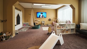 Uma sala de estar acolhedora com um espaço de brincadeiras, uma televisão e um sofá.