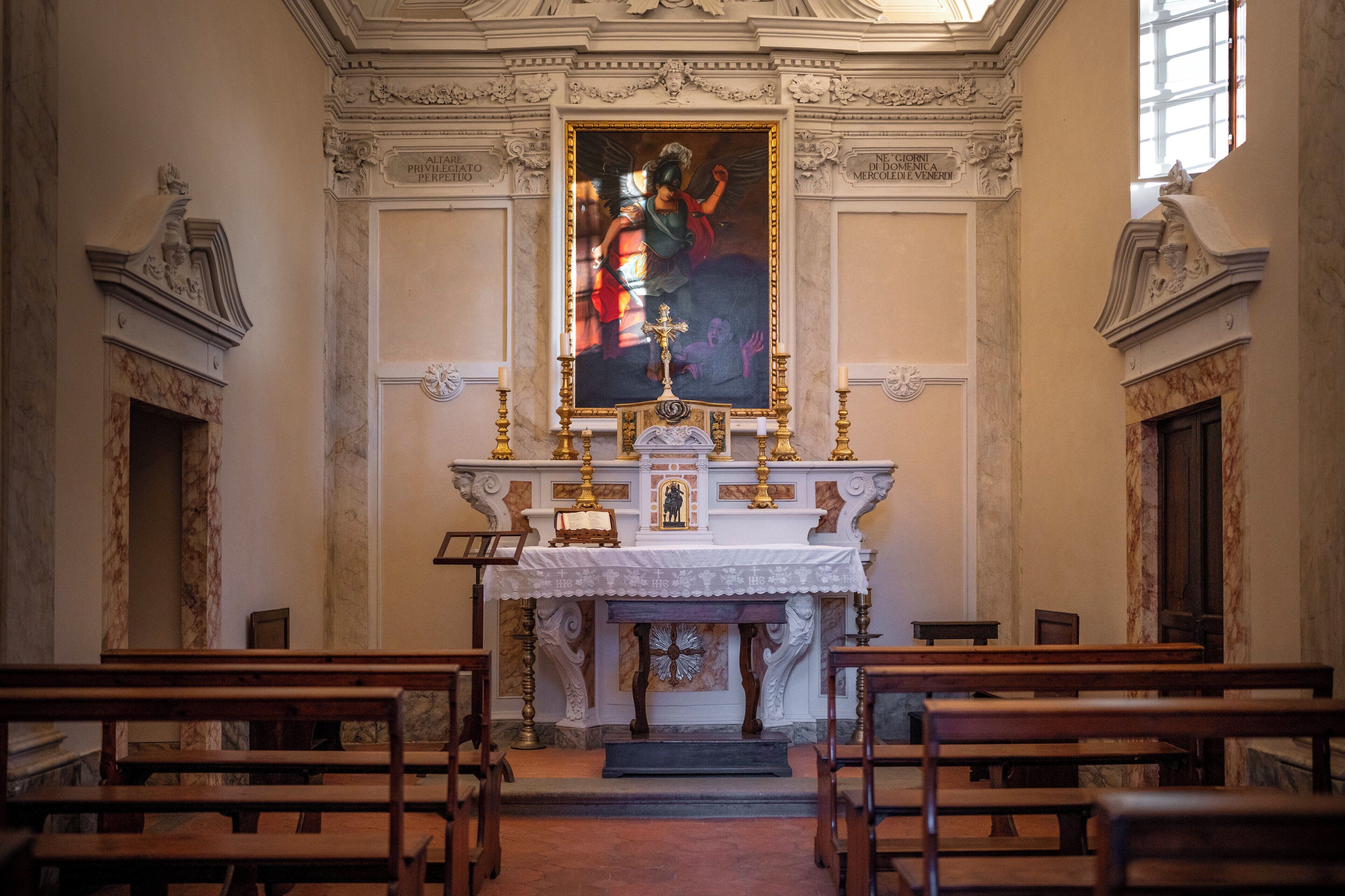 Interior de igreja ornamentado com altar central, bancos e uma grande pintura religiosa.