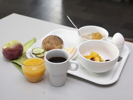Bandeja de café da manhã com muffin, maçã, copo de suco de laranja, tigela de frutas, xícara de café e tigela de cereal.
