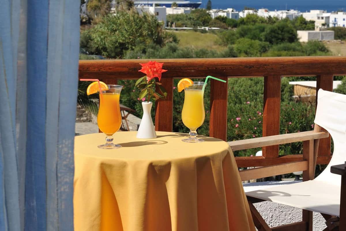 Uma mesa com duas bebidas, um vaso com flores e vista para o mar e edifícios.