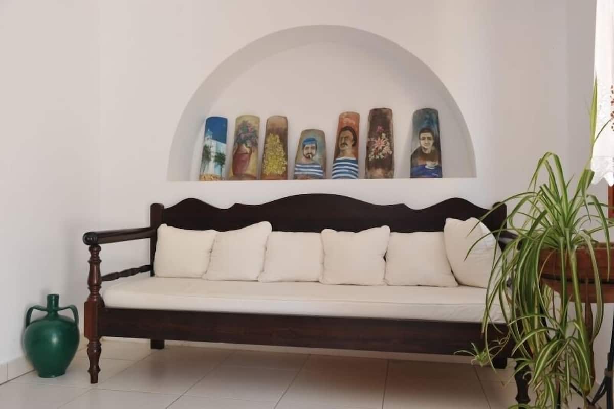 Um sofá de madeira escura com almofadas brancas, apoiado contra uma parede branca, sob uma janela em arco.