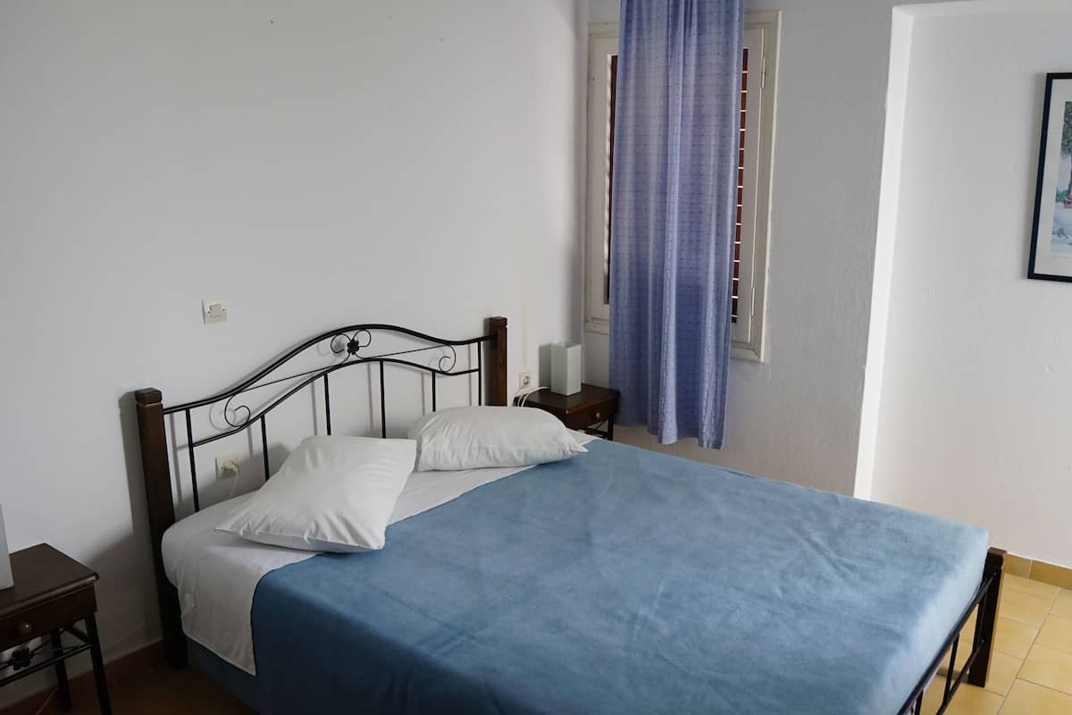 Quarto com uma cama de solteiro, mesa de cabeceira, janela com cortina e um quadro na parede.