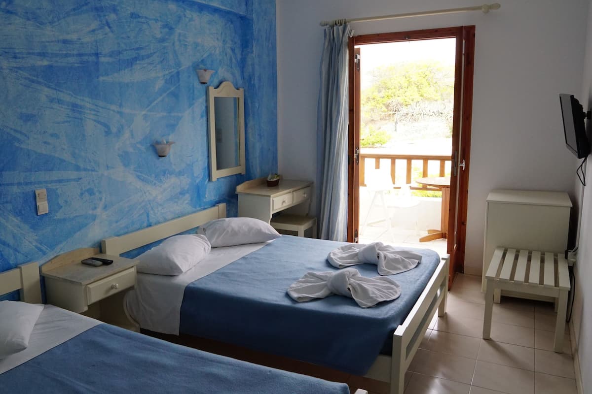 Quarto de hotel com duas camas, uma escrivaninha pequena, um espelho e varanda com grade de madeira.