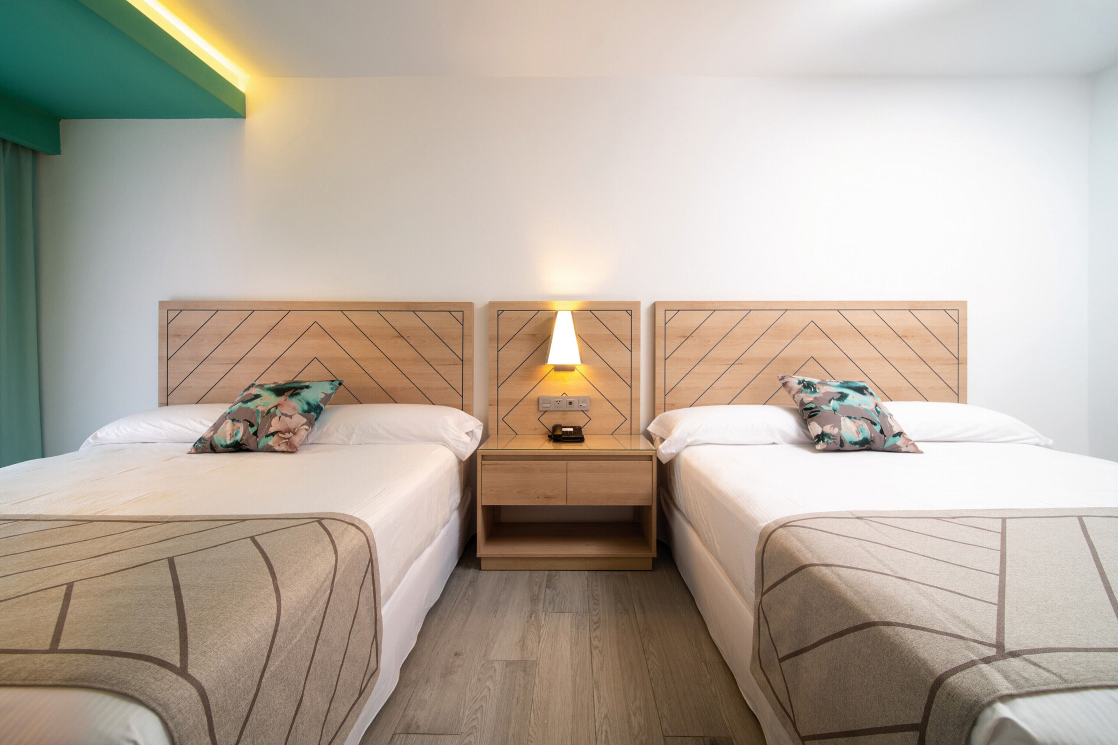 Quarto duplo com duas camas, cada uma com cabeceira de madeira e mesa de cabeceira com abajur.