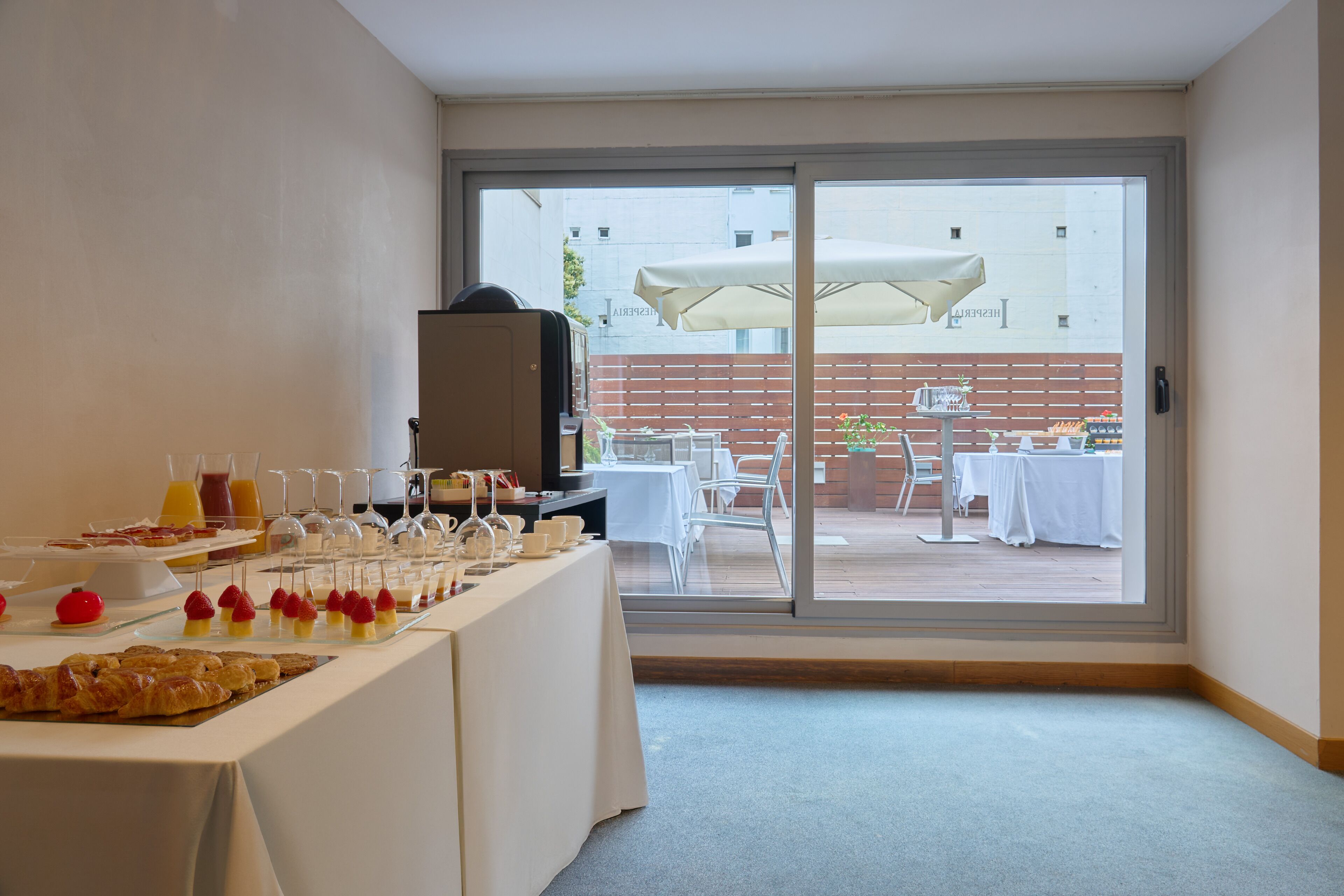 Buffet de café da manhã com diversos alimentos e bebidas, uma grande janela com vista para a área de estar externa.