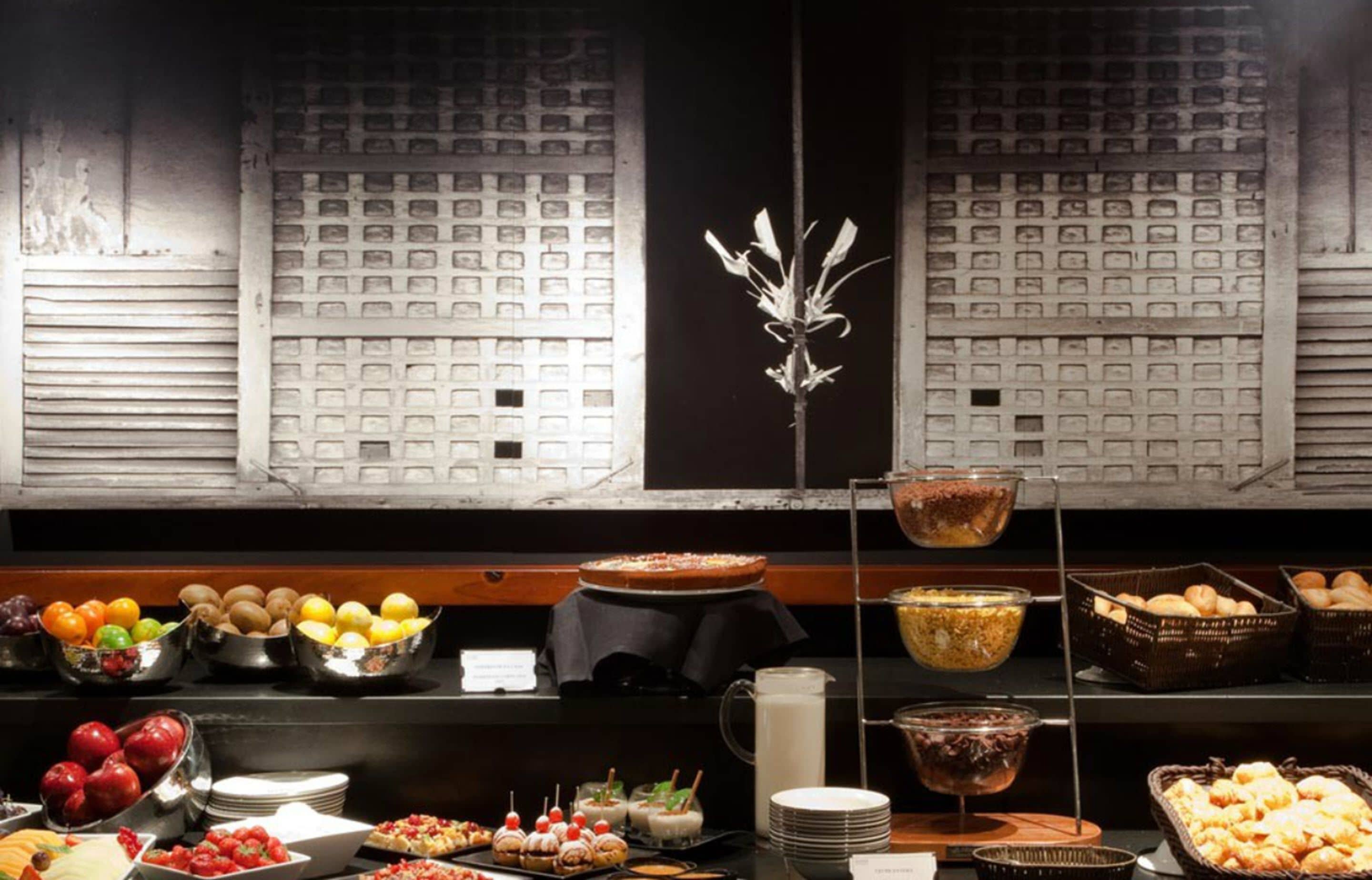 Buffet com diversos alimentos e parede decorativa com padrão geométrico.