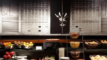 Buffet com diversos alimentos e parede decorativa com padrão geométrico.