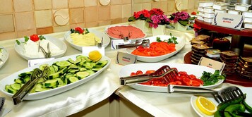 Buffet com diversas opções de comida, incluindo pepinos fatiados, tomates e carne.