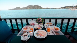 Uma mesa posta com itens de café da manhã e vista para o mar.