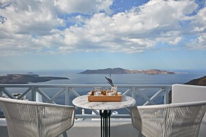 Terraço com cadeiras de vime e uma mesa disposta com uma bandeja de objetos, com vista para uma paisagem costeira e ilhas.
