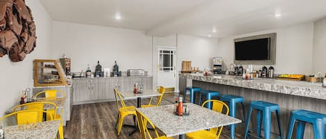 Cozinha moderna com bancadas de granito, área de refeições com cadeiras amarelas e um bar com banquetes azuis.