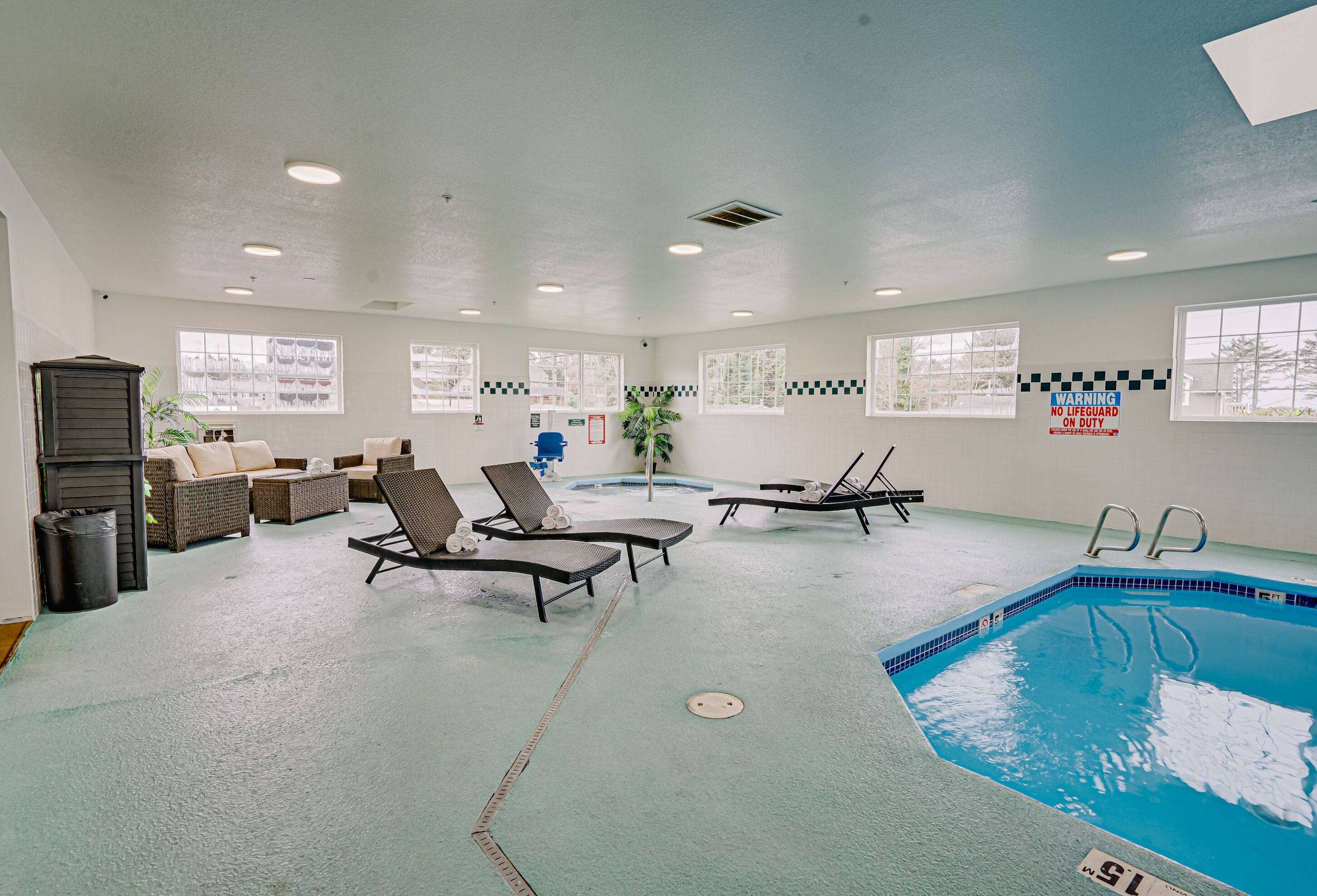Uma área de piscina com espreguiçadeiras, uma piscina pequena e um aviso na parede.