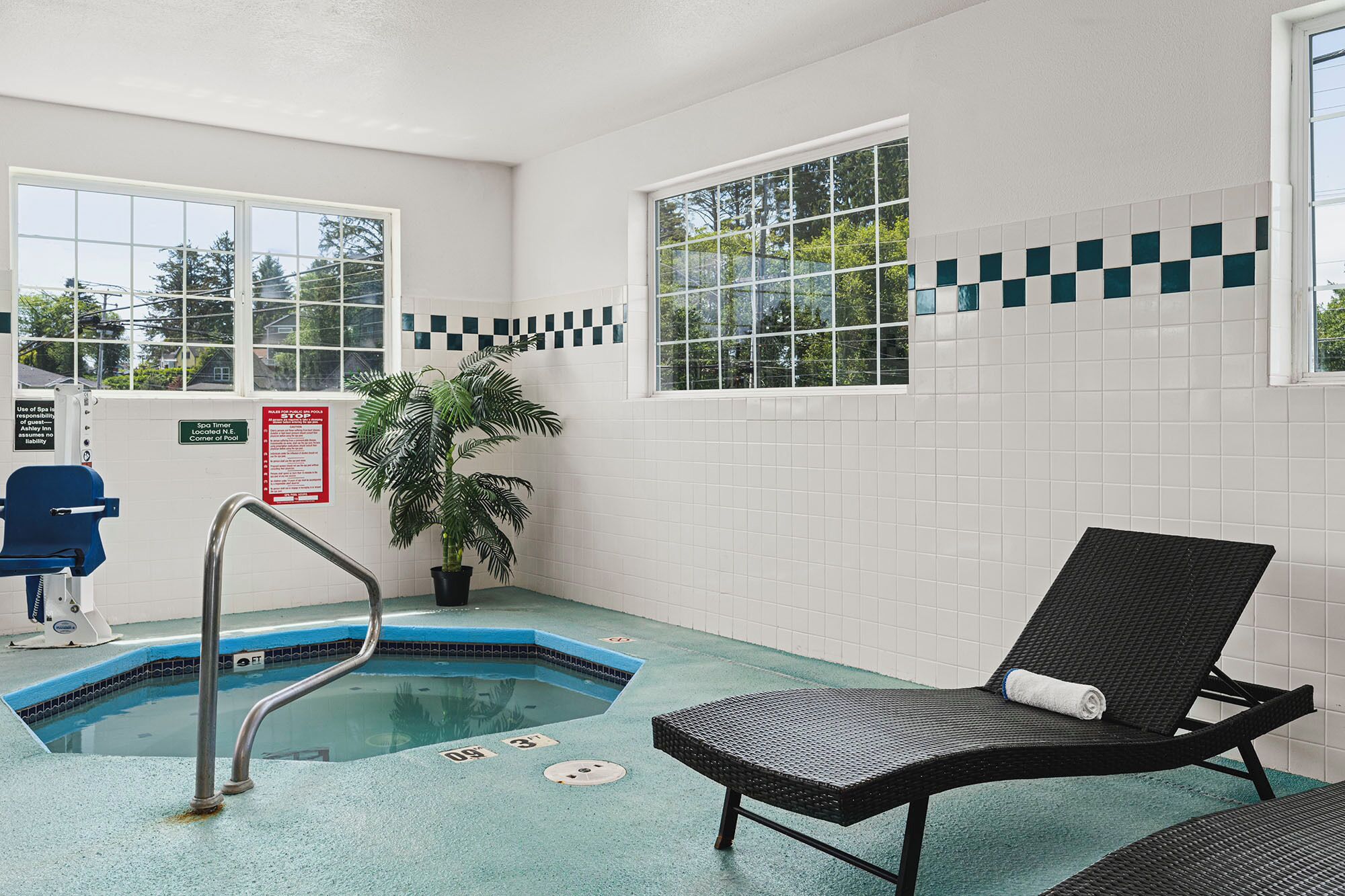 Uma área de spa com piscina, espreguiçadeira, planta em vaso e placa indicativa de horário do spa.