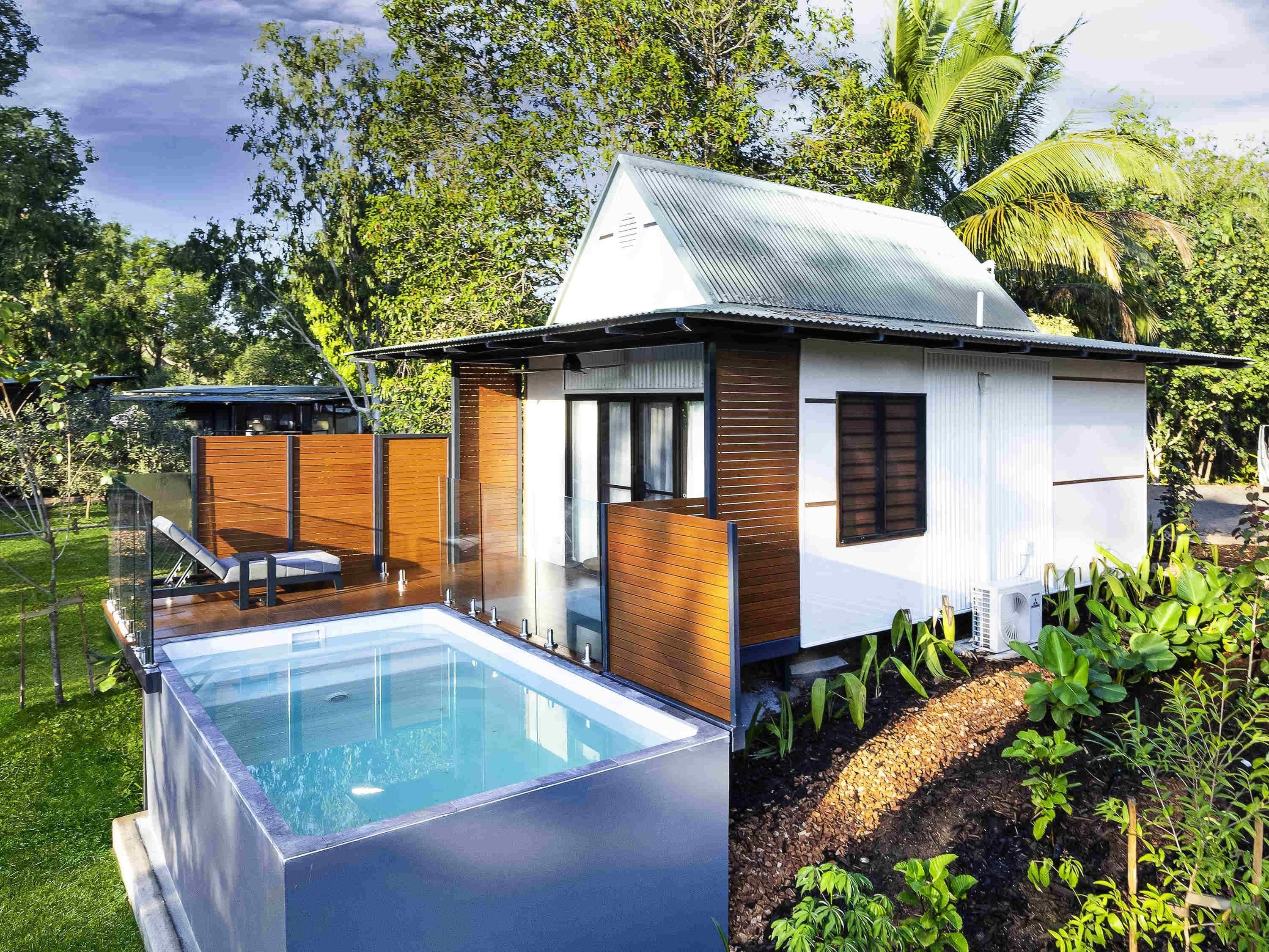 Uma casa moderna com piscina, deck de madeira e vegetação exuberante.