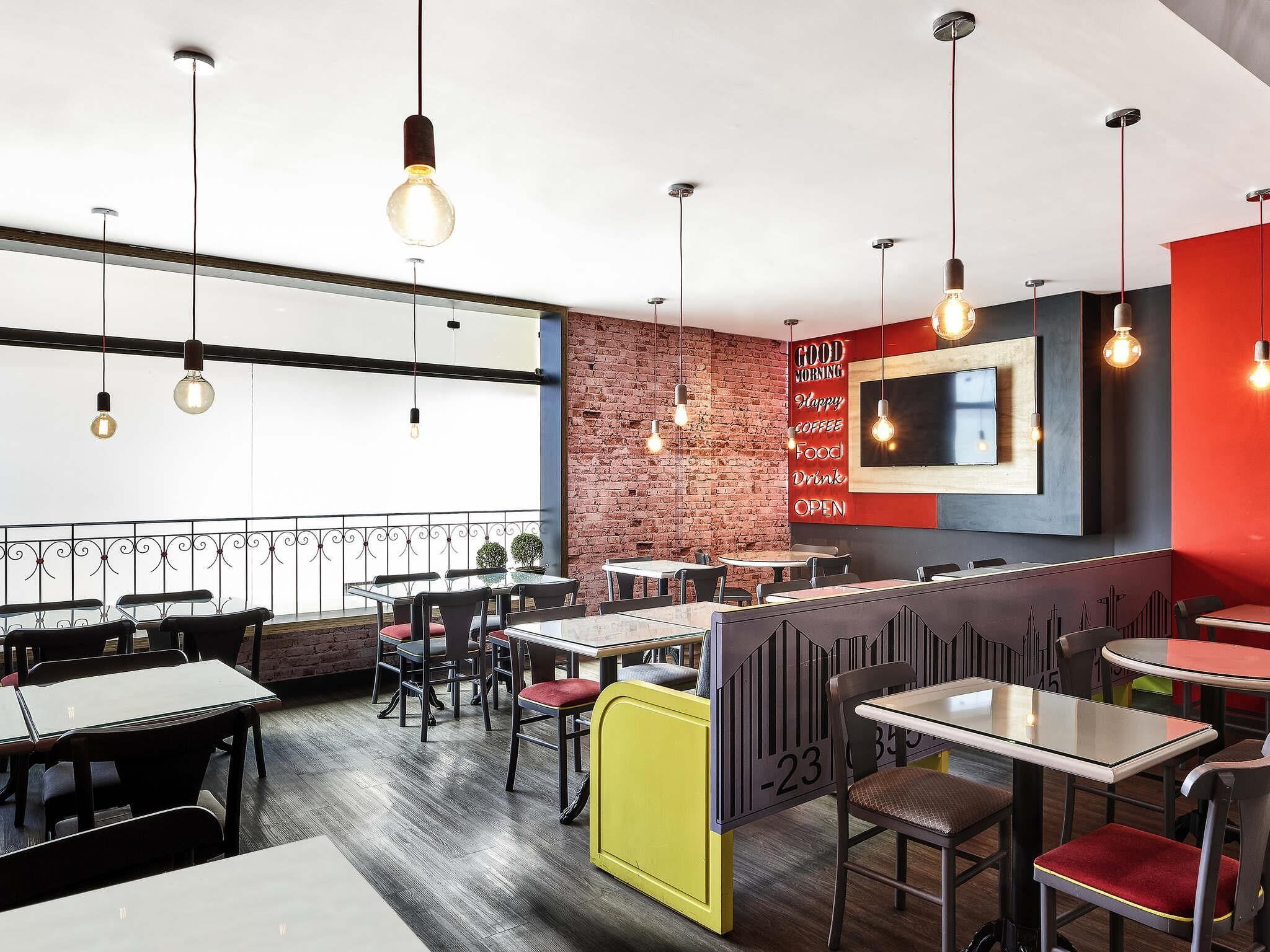 Um interior de restaurante moderno, com paredes de tijolo aparente, luminárias pendentes e diversas opções de assentos, incluindo cabines e mesas.