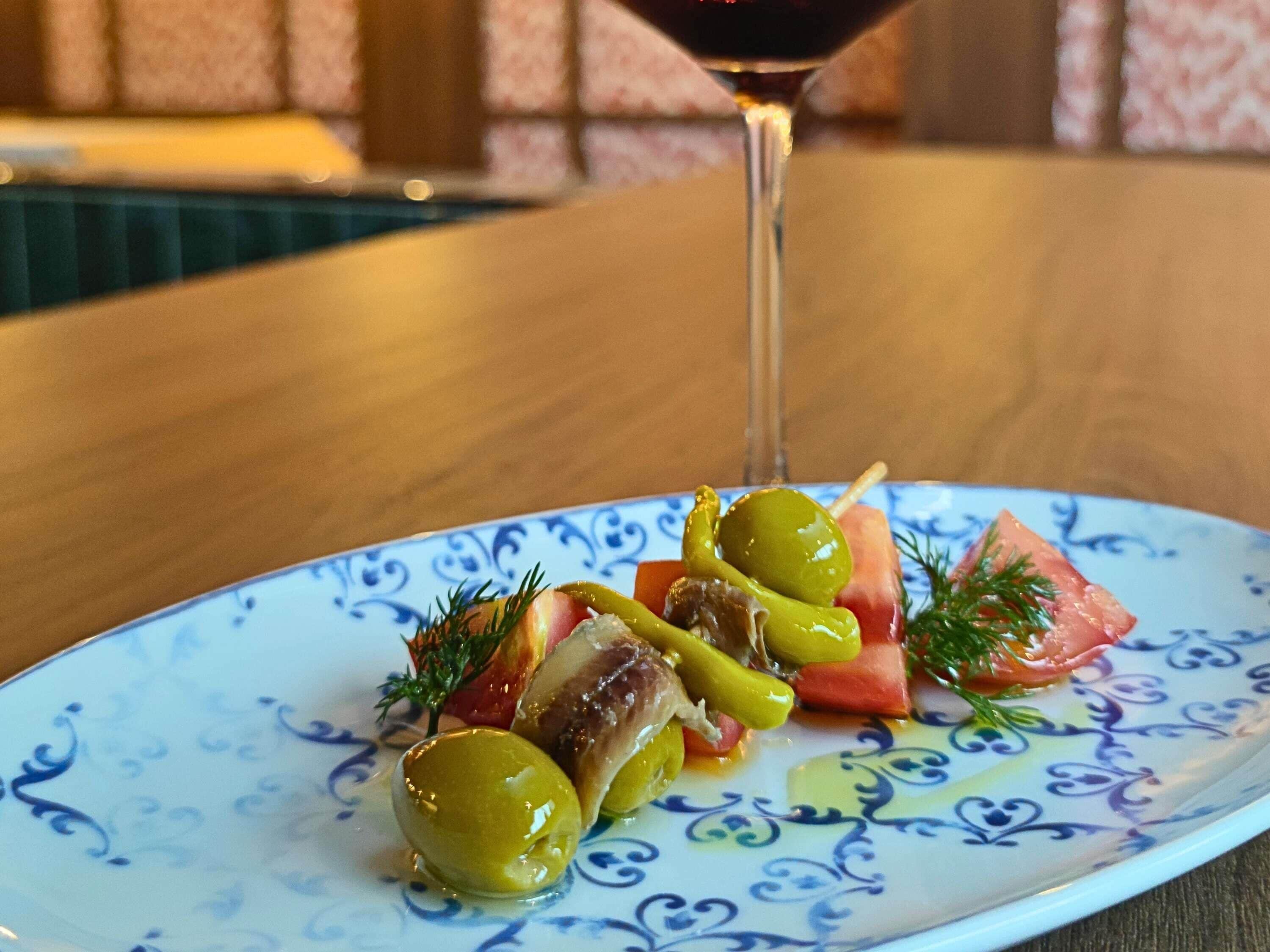Prato de comida com azeitonas, tomates e um copo de vinho tinto.