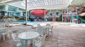 Parque aquático coberto com um grande tobogã, áreas de estar e um mural retratando uma paisagem tropical.