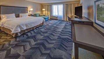 Quarto de hotel com uma cama grande, escrivaninha com televisão de tela plana, sofá e uma janela ampla com cortinas.