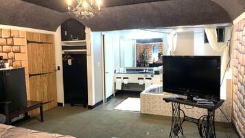Quarto pequeno com cama, televisão, máquina de costura e cozinha compacta.