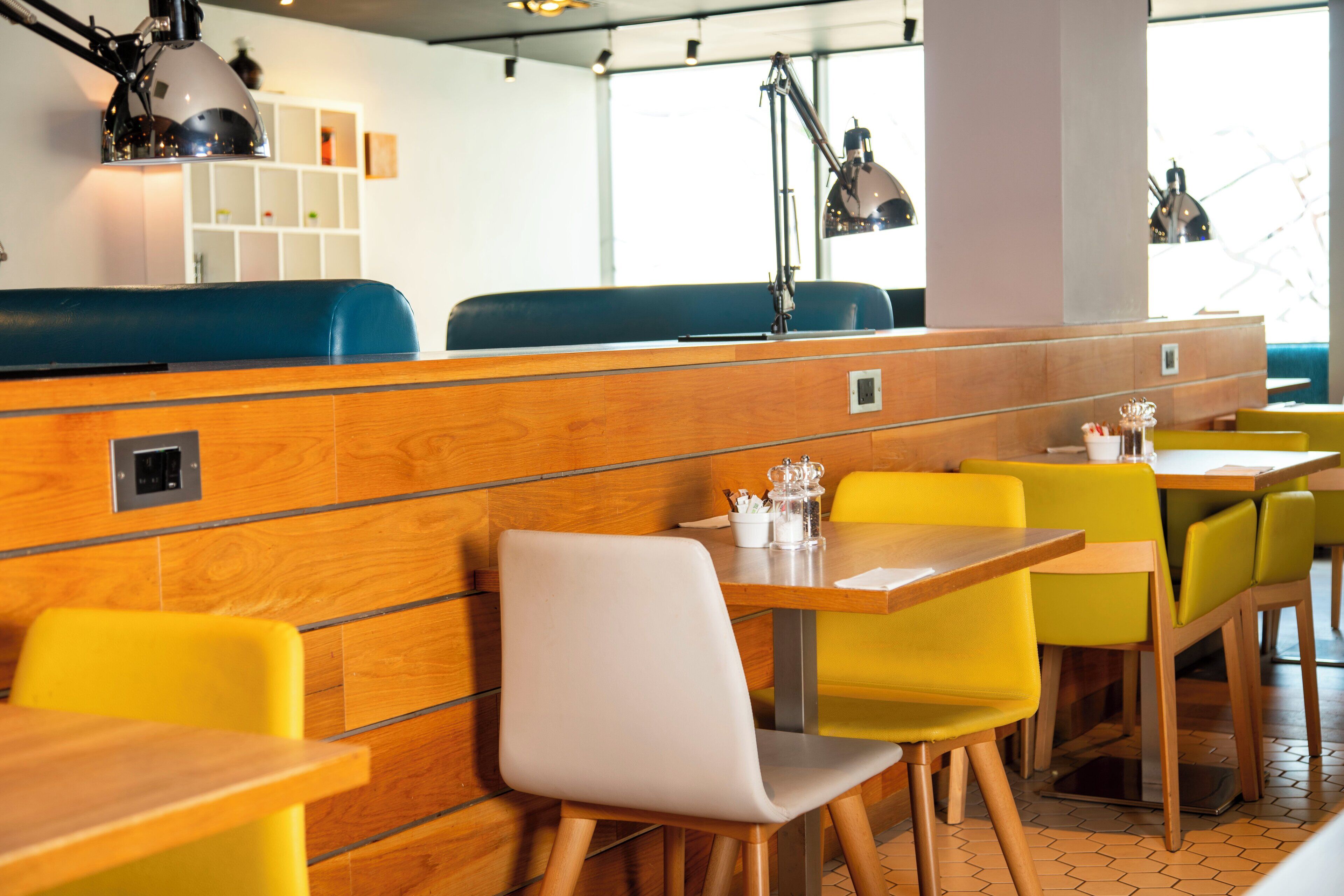 Restaurante com assentos em cabines de madeira, cadeiras amarelas e brancas, e mesas.