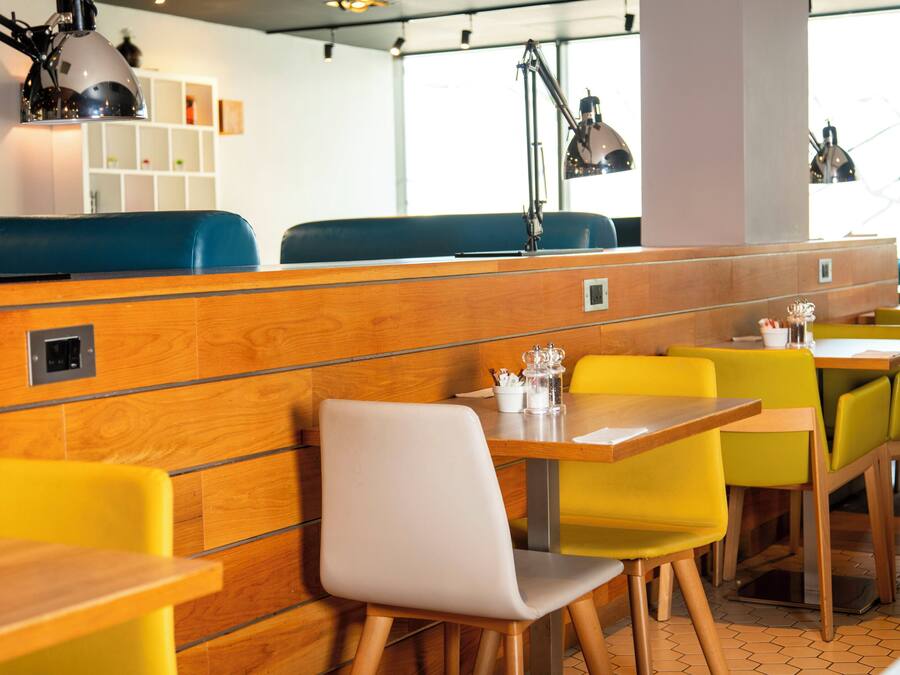 Restaurante com assentos em cabines de madeira, cadeiras amarelas e brancas, e mesas.
