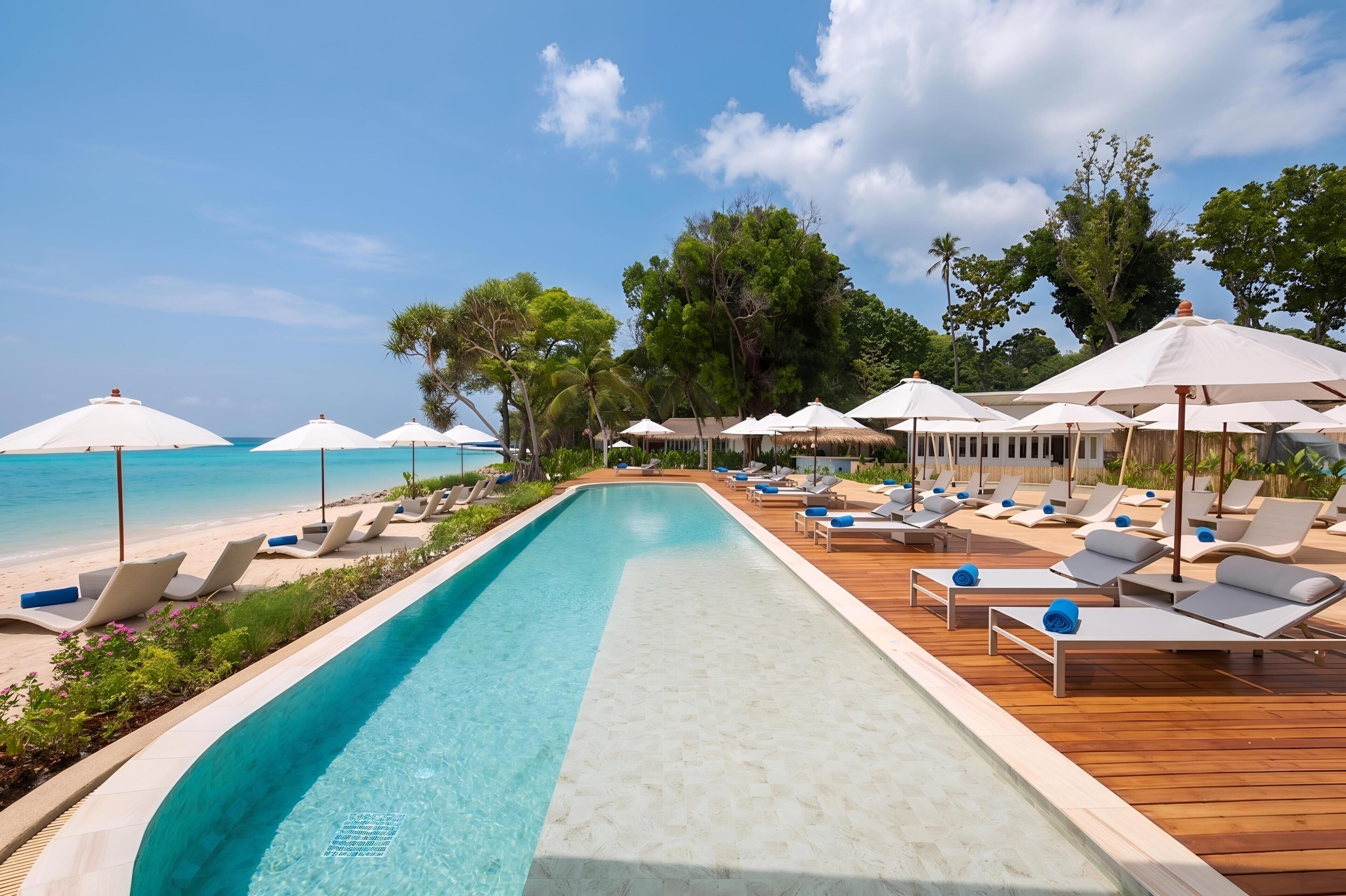 Área da piscina com espreguiçadeiras e guarda-sóis, piscina cristalina e vista para o mar.