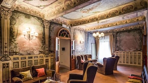 Quarto luxuoso com detalhes artísticos no teto, assentos confortáveis e luminárias elegantes.