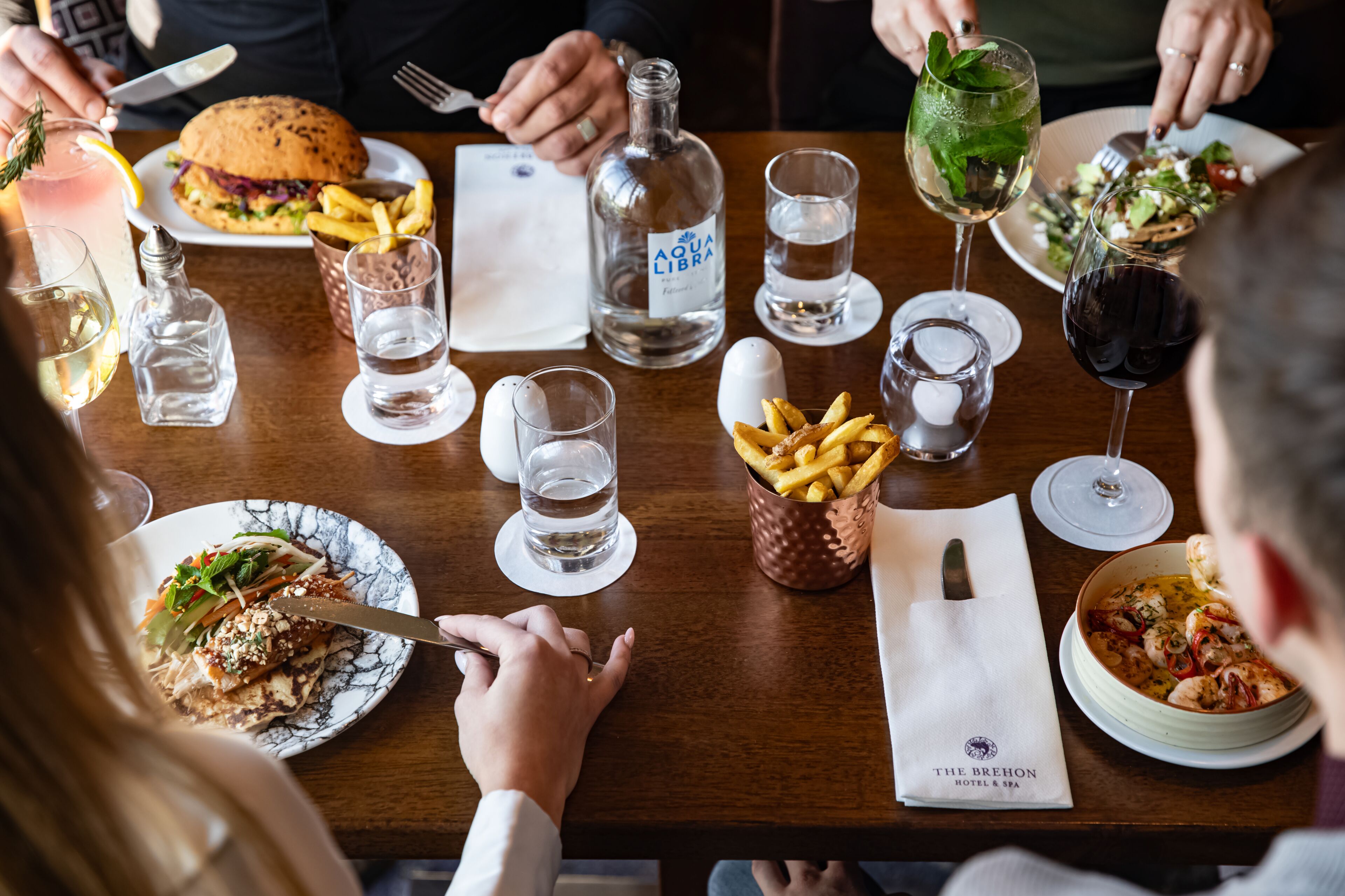 Uma mesa de jantar com diversos pratos, copos e uma garrafa com o rótulo 'AQUA LIBRA'.
