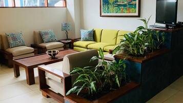 Uma sala de estar com sofá, poltronas, mesa de centro, televisão e um quadro na parede.