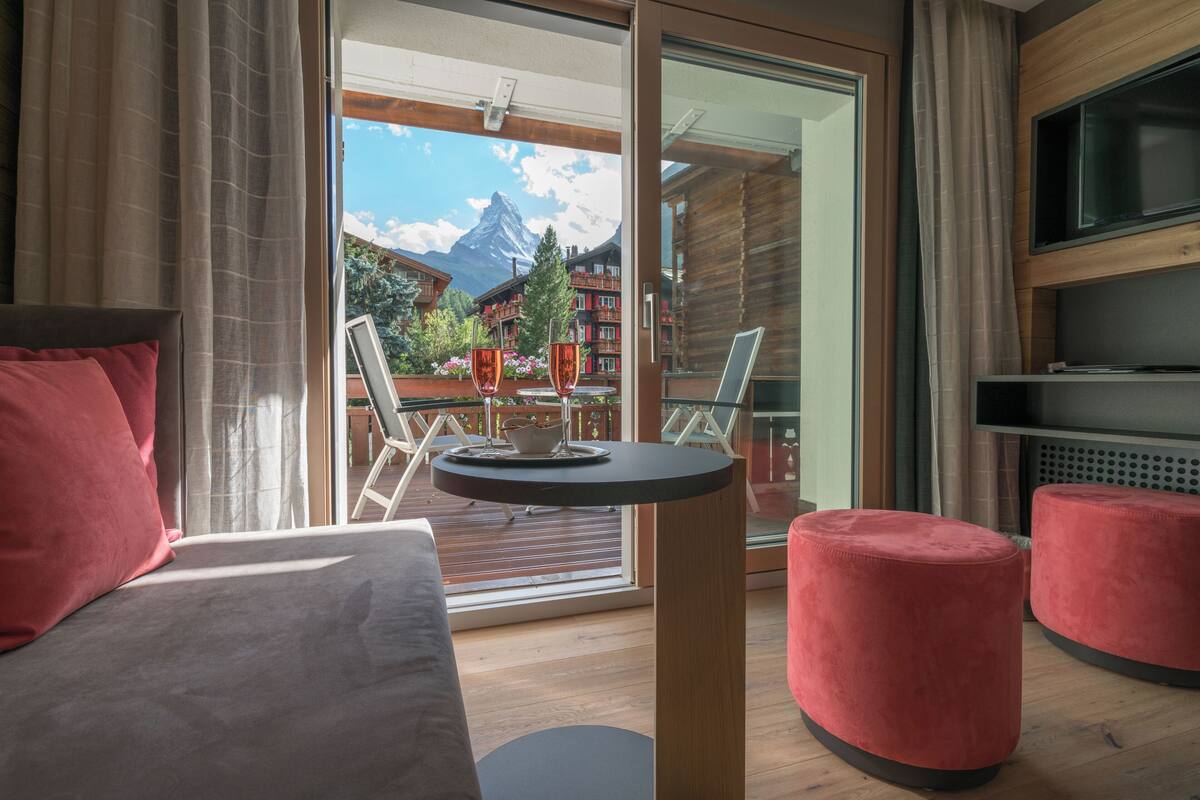 Quarto de hotel moderno com cama, uma mesa redonda e pufes vermelhos.