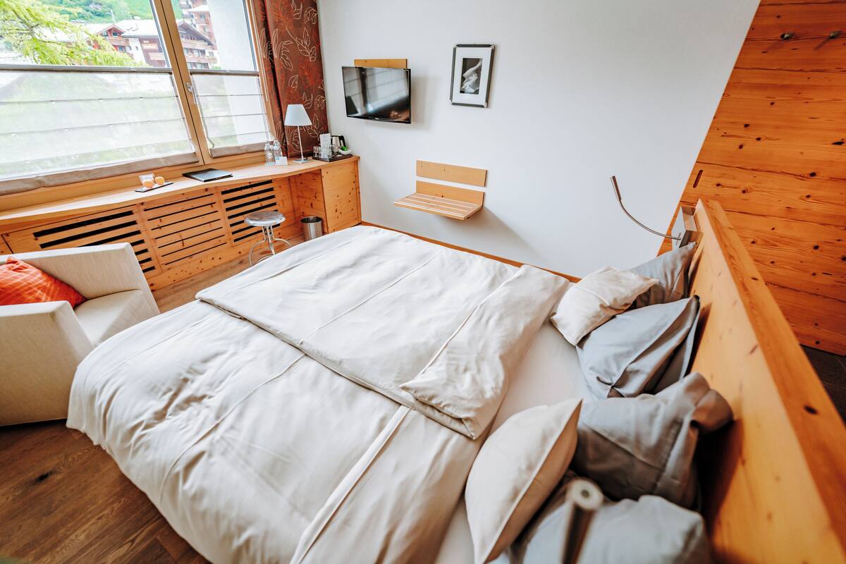 Quarto com cama de madeira, uma escrivaninha e uma janela.