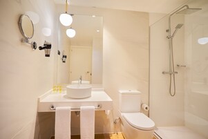 Uma casa de banho moderna com uma sanita, chuveiro, um lavatório redondo e um espelho com luzes.
