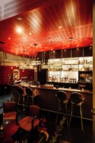 Uma área de bar com teto vermelho, banquetas e uma adega bem abastecida.