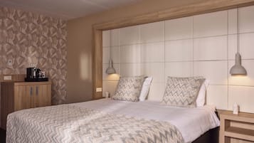 Quarto de hotel bem organizado, com uma cama grande, duas mesinhas de cabeceira, um criado-mudo de madeira, papel de parede estampado e uma luminária fixada na parede.