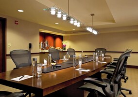 Uma sala de conferência com uma mesa grande, cadeiras, um espaço para café e um lustre decorativo.