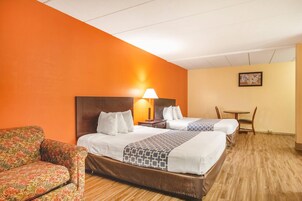Quarto de hotel com duas camas, um sofá, um abajur, uma mesa e uma cadeira.