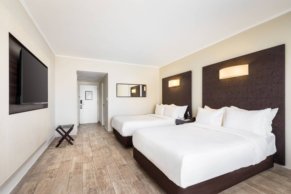 Quarto de hotel com duas camas, televisão, espelho e porta para outro cômodo.