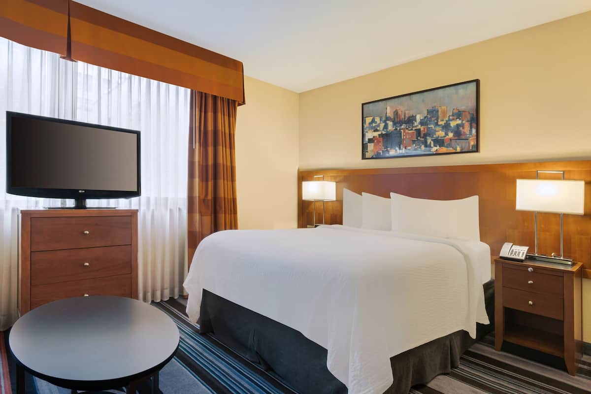 Quarto de hotel com uma cama grande, televisão de tela plana, escrivaninha e um quadro na parede.