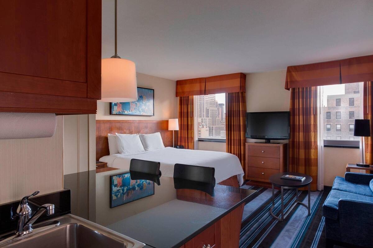 Quarto de hotel com cama, escrivaninha, televisão e vista para a cidade.