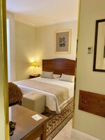Quarto de hotel com uma cama grande, uma mesa de cabeceira, uma luminária, um quadro na parede e um termostato.