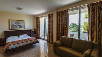 Quarto de hotel com cama, sofá, mesa de cabeceira, abajur e janela com cortinas.