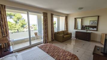 Quarto de hotel com uma cama grande, um sofá, um aparador, um espelho e uma varanda com vista para árvores e edifícios.