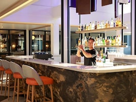 Uma área de bar com um bartender, um balcão de mármore e prateleiras com garrafas.