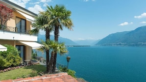 Um hotel com varanda com vista para um lago, palmeiras e montanhas ao fundo.